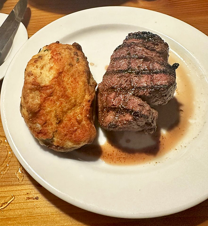 This perfectly grilled filet mignon with its glistening sear marks sits beside a baked potato that's practically bursting with anticipation.