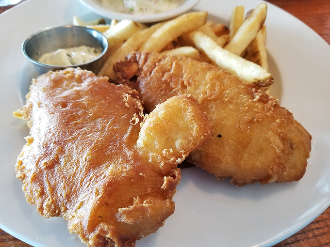 Golden-battered fish that shatters at first bite, revealing flaky perfection beneath – this is what fish and chips dreams are made of.