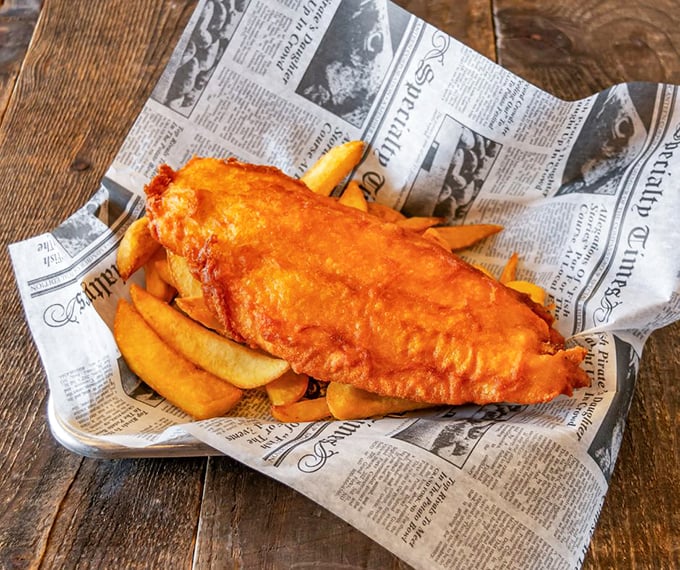 Golden, crispy batter hugging flaky white fish atop chunky chips—newspaper wrapping completes this authentic British masterpiece.