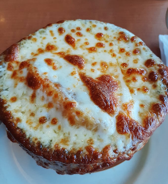 This isn't just cheese on soup—it's a golden-brown cathedral dome of bubbling perfection that demands a moment of reverent silence before diving in.