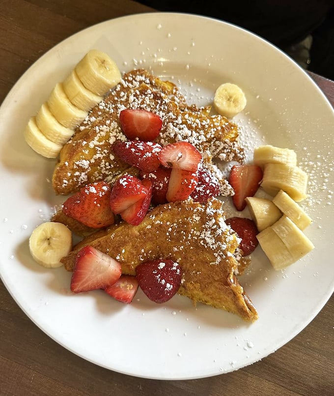 French toast that doesn't just arrive—it makes an entrance. Crowned with fresh strawberries and bananas, it's breakfast royalty dusted with powdered sugar confetti.