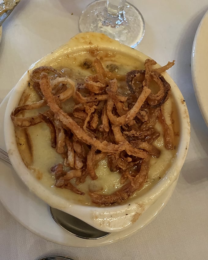 The legendary French onion soup arrives like a work of art – a bubbling cauldron of perfectly caramelized onions beneath a golden crown of cheese.