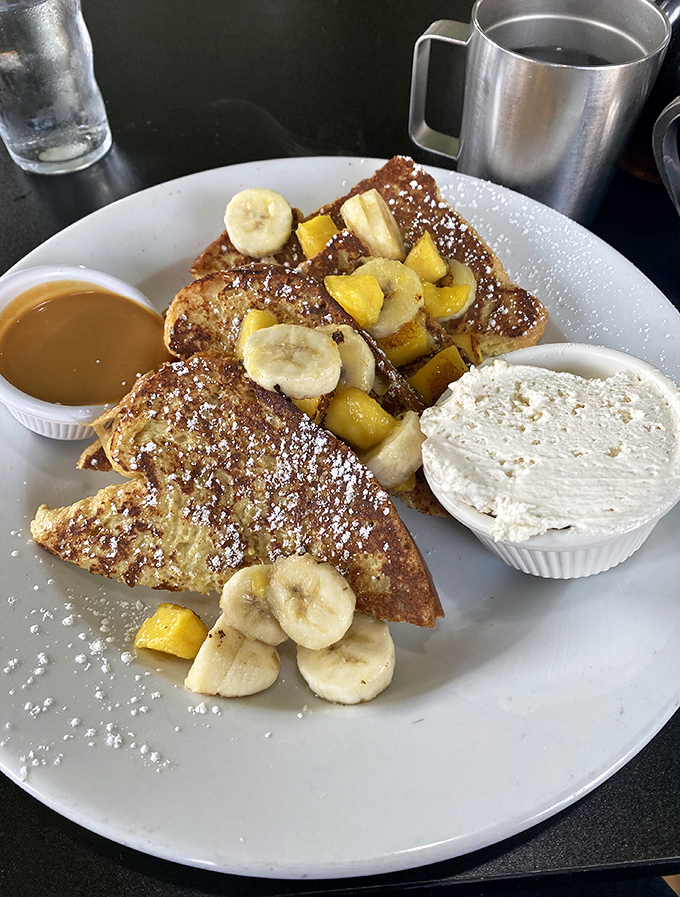 Behold the French toast that dreams are made of – golden triangles crowned with fresh fruit and powdered sugar perfection.