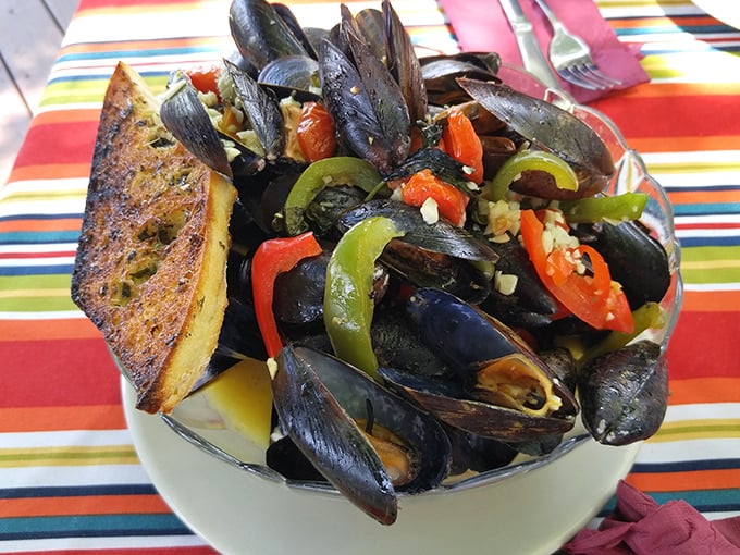 These aren't just mussels—they're little black submarines of joy navigating through a sea of garlicky, buttery goodness. The toasted bread? Your perfect rescue vessel.