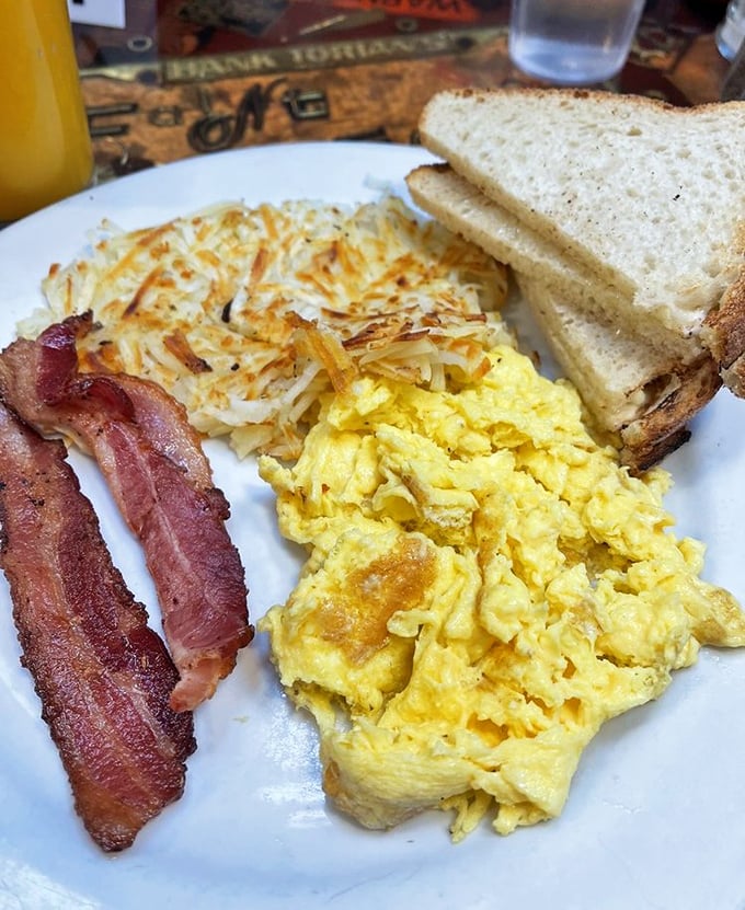 Breakfast perfection on a plate: golden scrambled eggs, crispy hash browns, and bacon cooked just right—the holy trinity of morning satisfaction.