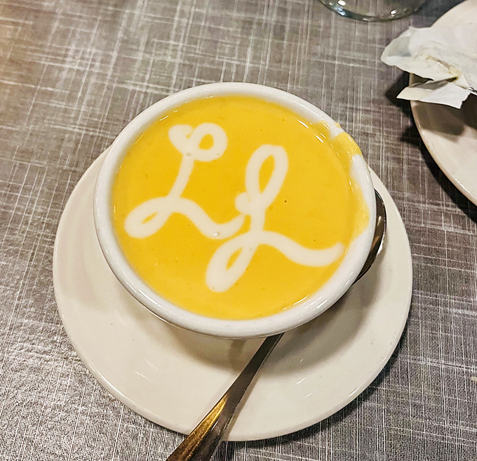 The bisque arrives with its own signature—a creamy yellow canvas where the restaurant's initials promise flavor in every spoonful.