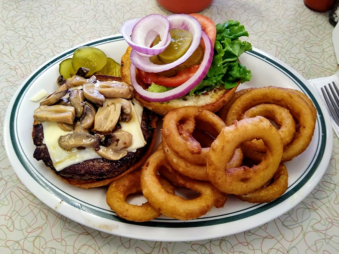 A burger that means business, flanked by onion rings that could double as golden halos. This isn't just lunch—it's a commitment to happiness.