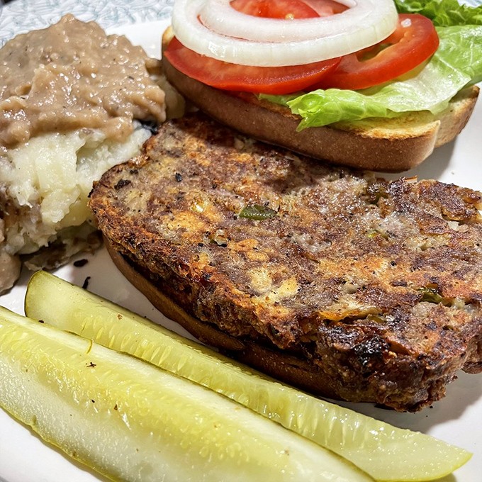 This meatloaf doesn't just sit on the plate—it commands attention with its perfectly caramelized exterior and hearty presence alongside real mashed potatoes.