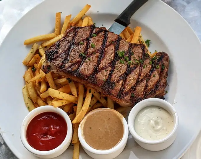This steak doesn't just arrive at your table—it makes an entrance, complete with perfect grill marks and a trio of sauces standing at attention.