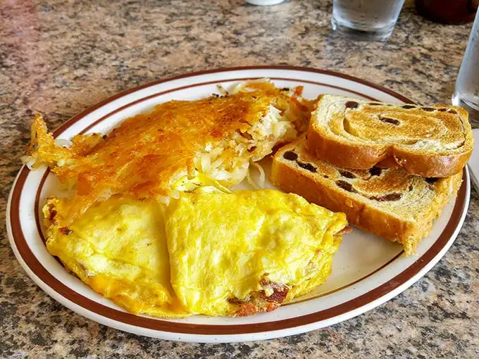 Behold the omelet in its natural habitat—perfectly executed, cheese pulling a disappearing act at the edges, with crispy hash browns standing guard.