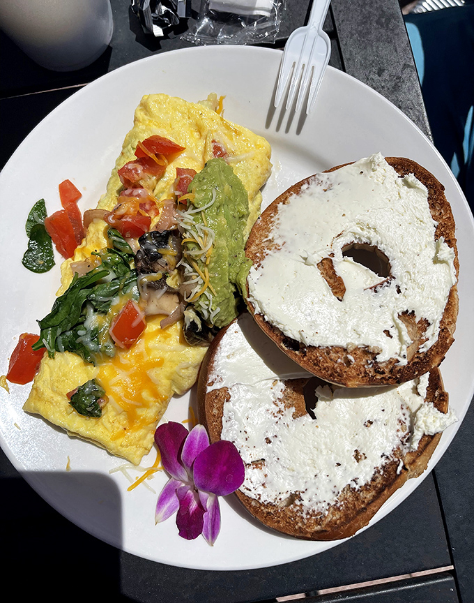A perfect omelet meets its soulmate: a generously schmeared bagel. That purple orchid isn't just garnish—it's celebrating this beautiful union.
