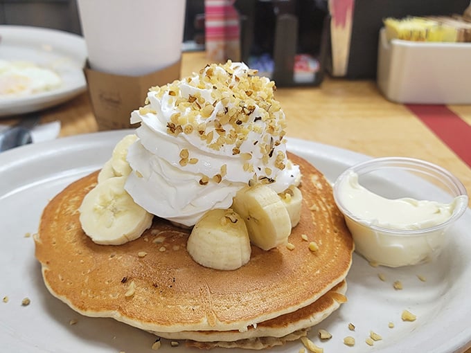 Pancakes crowned with whipped cream, bananas, and what appears to be walnut crumble—proof that breakfast can indeed be the most important art of the day.