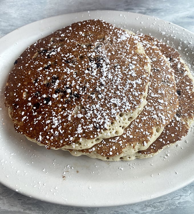Golden-brown pancakes dusted with powdered sugar—the kind that make you wonder why anyone bothers with fancy brunch when diners perfected breakfast decades ago.