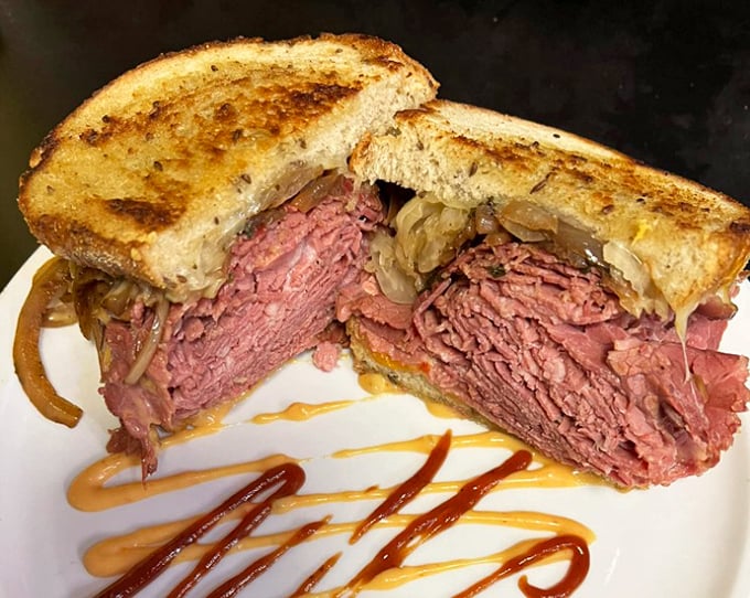 This pastrami sandwich isn't just stacked—it's an architectural marvel that requires both hands, several napkins, and absolutely zero shame.