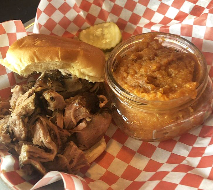 Pulled pork perfection in its natural habitat—checkered paper with a side of baked beans. This sandwich doesn't need a fancy plate to impress.