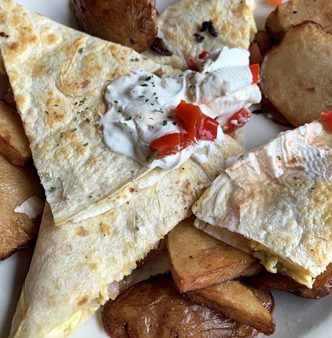 Behold the star of our show—golden-brown tortilla triangles revealing their molten cheese treasure, served with a dollop of sour cream that's practically winking at you.