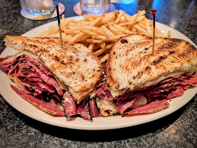 The Reuben in its natural habitat – gloriously stacked, perfectly toasted, and flanked by golden fries. This isn't a sandwich; it's an architectural masterpiece.
