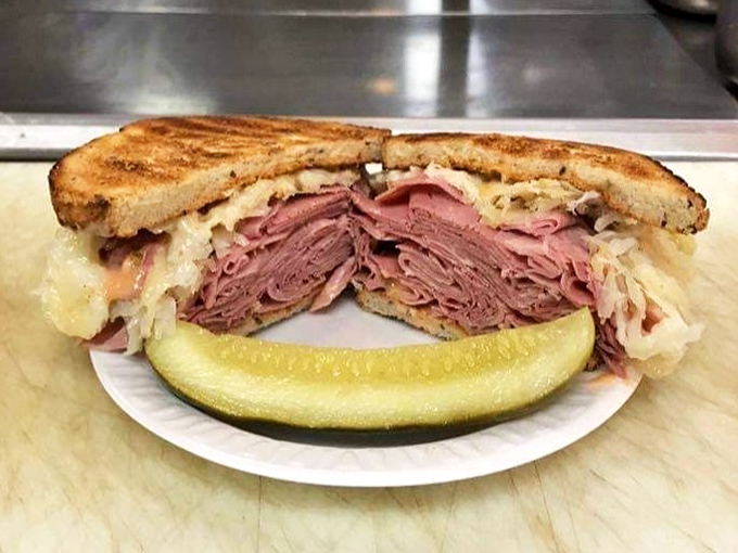 Behold the Reuben in its natural habitat—a mountain of corned beef flanked by sauerkraut and Swiss, with a pickle standing guard.