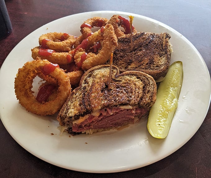 That perfect Reuben sandwich with golden onion rings isn't just lunch—it's therapy on a plate, complete with the mandatory pickle spear standing guard.