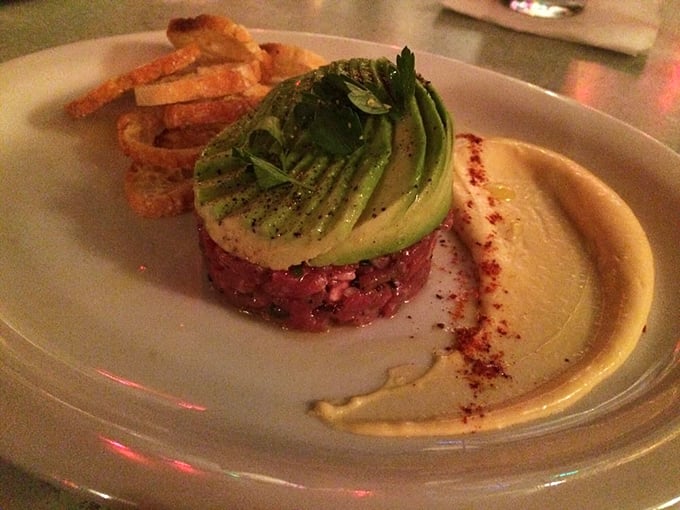 Poole's steak tartare arrives like edible artwork—ruby-red beef crowned with creamy avocado that'll make you question why you ever bothered cooking meat.