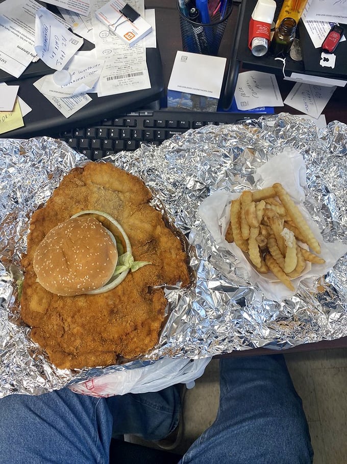 Behold the tenderloin in its natural habitat—sprawled majestically across aluminum foil like it's sunbathing on a metallic beach, making that regular-sized bun look like a tiny hat.