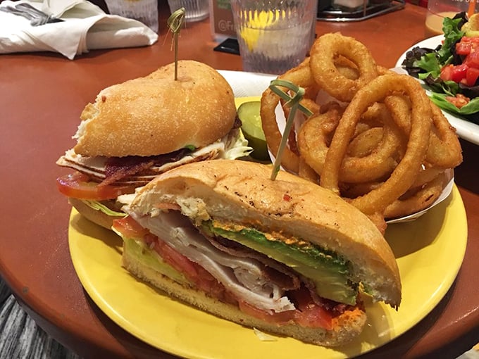 The legendary club sandwich arrives like architecture on a plate – perfectly stacked layers of savory goodness flanked by golden onion rings.