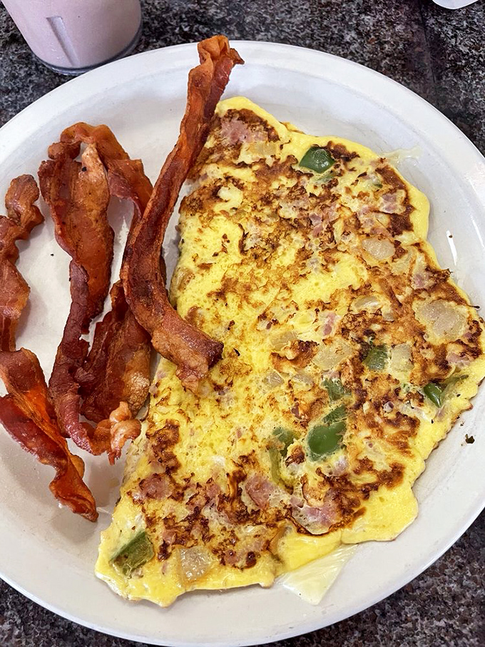 Behold the Western omelet in all its glory—a golden canvas of perfectly cooked eggs studded with ham, peppers, and onions. Bacon standing guard nearby.