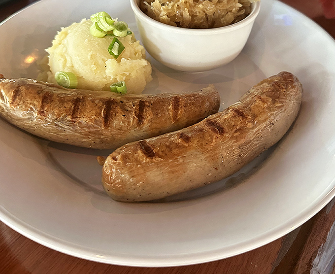 Two perfectly grilled bratwursts nestled beside creamy mashed potatoes and sauerkraut—comfort food that speaks a universal language of deliciousness.