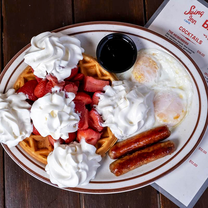 Breakfast nirvana: golden waffles crowned with strawberries and whipped cream, flanked by eggs and sausage – the breakfast equivalent of winning the lottery.