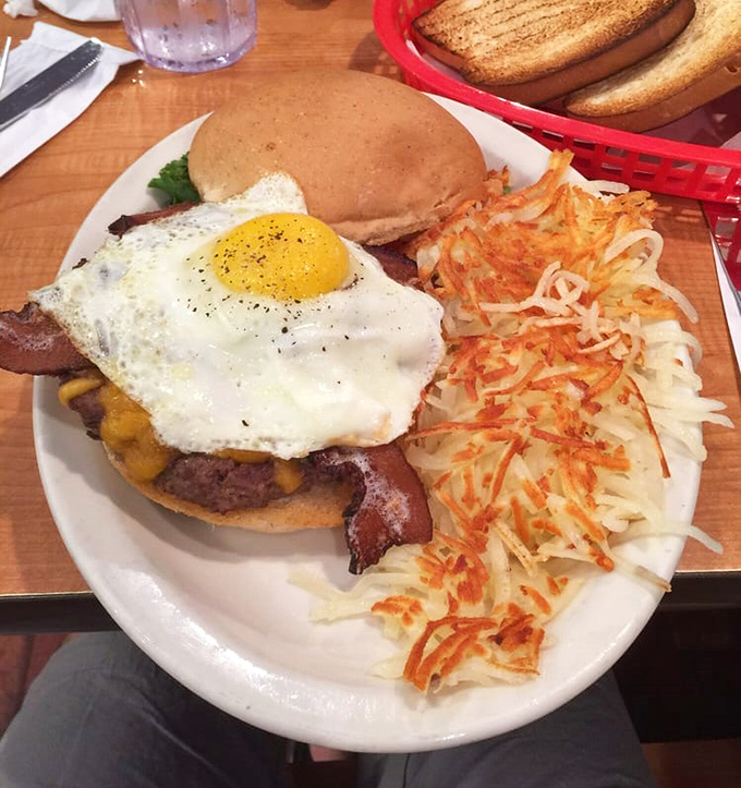 Breakfast architecture at its finest—a tower of burger, bacon, and sunny-side-up egg that makes your avocado toast look like amateur hour.