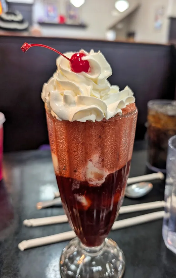 The cherry float isn't just a drink, it's architectural poetry—layers of fizzy cherry goodness supporting a cloud of whipped cream, all crowned with that essential maraschino cherry.