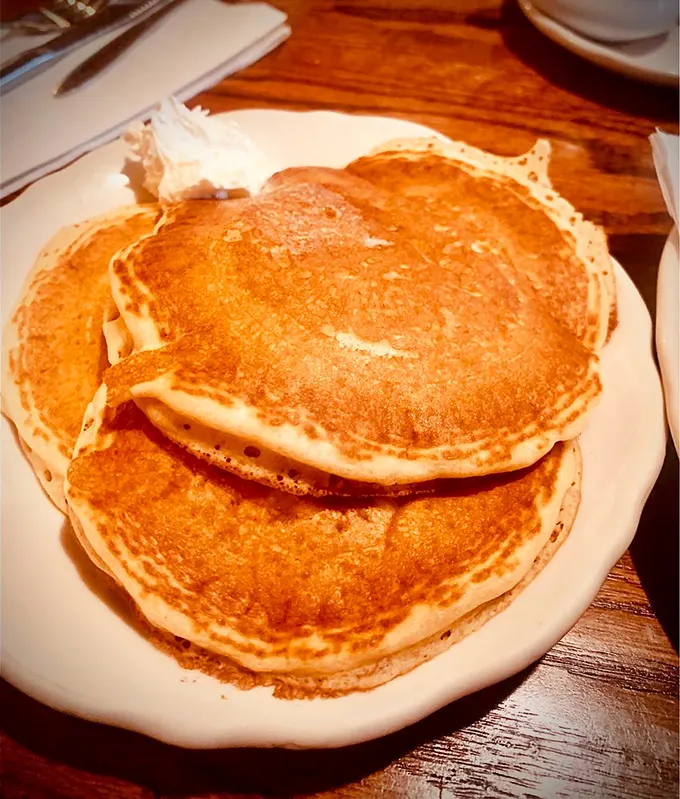 Golden-brown perfection stacked three high – these aren't just pancakes, they're edible sunshine that would make even morning grumps smile.