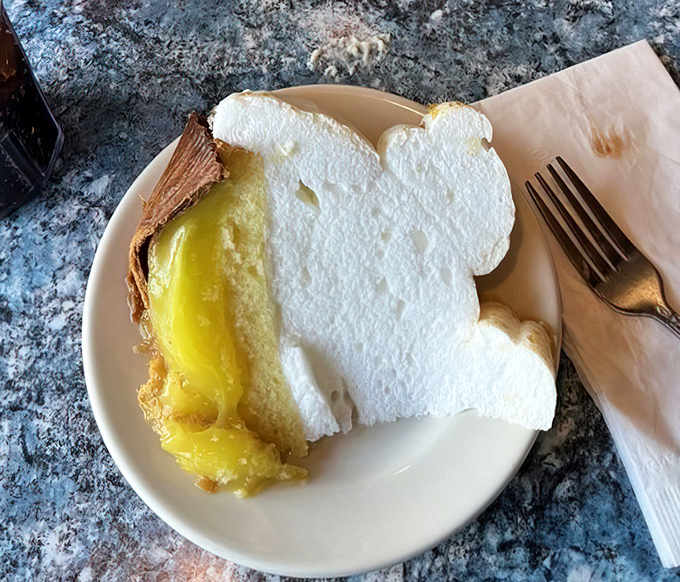 Lemon meringue pie that defies gravity with clouds of pillowy meringue floating above sunshine-yellow filling—a slice of heaven on a plain white plate.