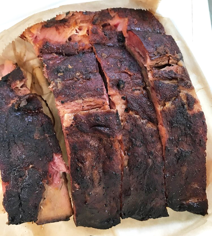 These ribs aren't just cooked, they're transformed—that dark bark protecting tender meat underneath is BBQ alchemy at its finest.