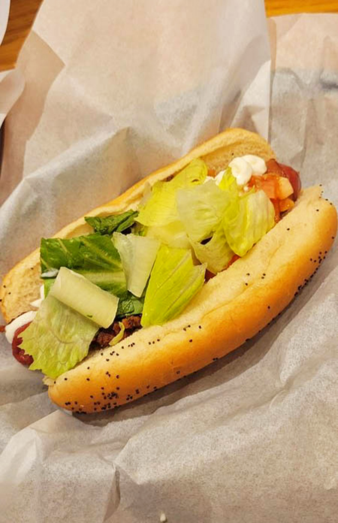 Fresh lettuce and tomato bring a crisp counterpoint to this hot dog's savory depths—proof that balance exists even in comfort food paradise.