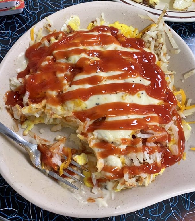Breakfast architecture at its finest – layers of eggs, hash browns, and cheese crowned with a zigzag of ketchup that says "Good morning, indeed!"