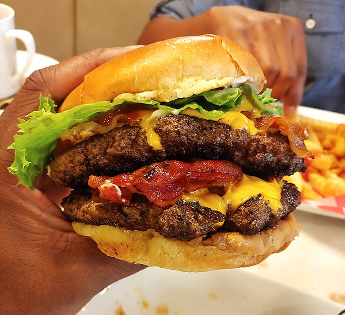 Behold the burger that makes vegans question their life choices—stacked high enough to require jaw exercises before attempting.