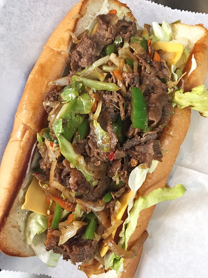 Behold the cheesesteak in its natural glory—overflowing with meat, veggies, and melty cheese. This isn't a sandwich; it's an architectural marvel.