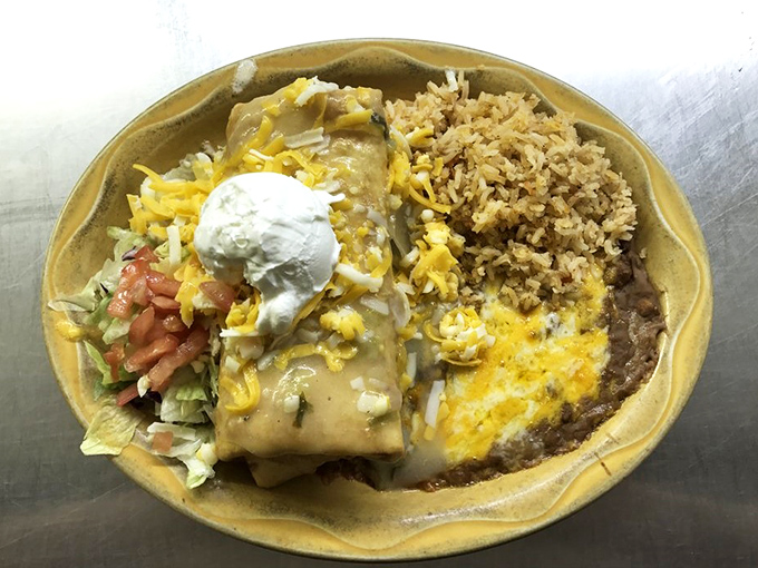 The chimichanga arrives like royalty on a golden plate, topped with a crown of sour cream and surrounded by its loyal subjects: rice and beans.