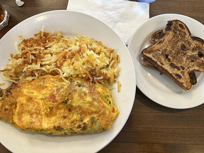 This isn't just an omelette—it's a masterpiece of morning architecture with perfectly crisp hash browns and raisin toast that deserves its own fan club.