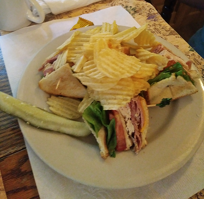 The club sandwich arrives like an architectural marvel—layers of Virginia ham and fresh vegetables flanked by a guard of perfectly crisp chips.