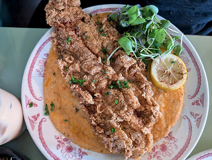 The Fish N Grits arrives like edible artwork – crispy catfish perched atop creamy grits, with that roasted pepper sauce creating a pool of pure flavor bliss.