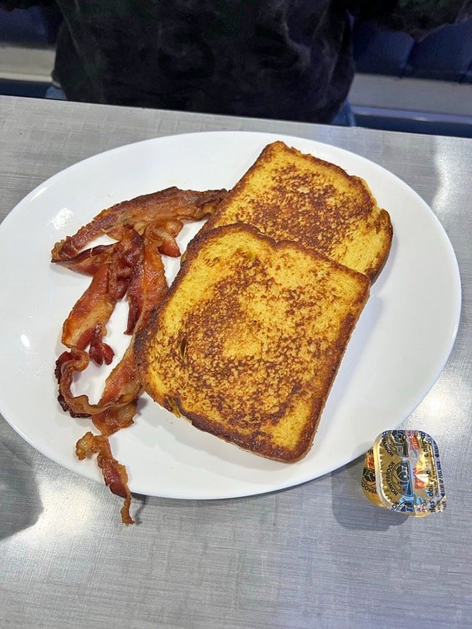 Golden-brown French toast with a side of perfectly crispy bacon – breakfast's greatest hits album on a single white plate.