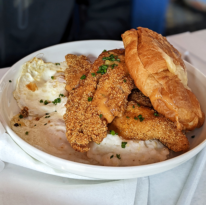 Crispy catfish perched atop creamy grits like it owns the place, with a golden-brown crust that crackles with each bite. The croissant is just showing off.