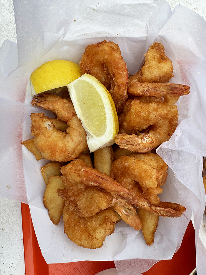 Golden-battered shrimp and fries nestled in paper—seafood at its most honest. That lemon wedge isn't just garnish; it's essential equipment.