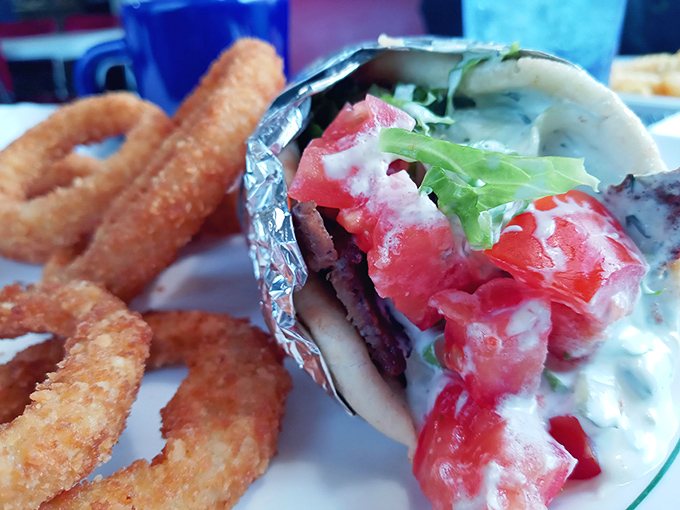 This isn't just a gyro—it's edible architecture. Crispy onion rings standing guard beside a sandwich that requires both hands and several napkins.
