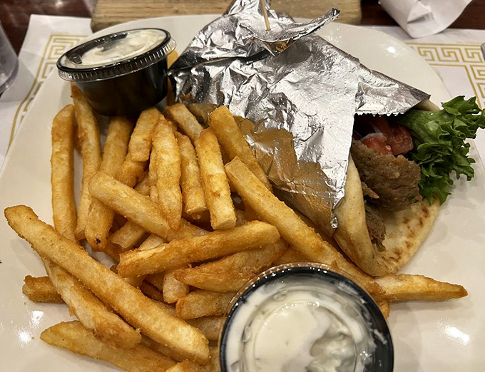 The gyro wrap arrives like a foil-wrapped present, flanked by golden fries standing at attention. Dipping sauce on standby for the inevitable french fry reconnaissance mission.