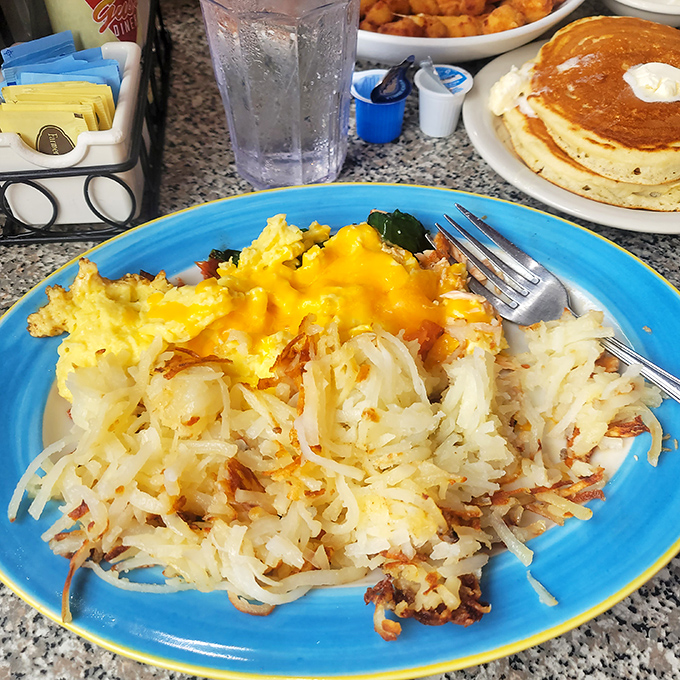 Golden hash browns that crackle with each bite, crowned with melted cheese and paired with fluffy scrambled eggs – breakfast nirvana on a blue plate.