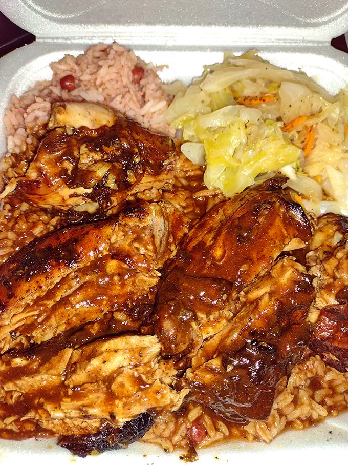 Jerk chicken that falls off the bone, nestled beside perfectly seasoned rice and cabbage—a holy trinity of Caribbean comfort on a humble styrofoam plate.