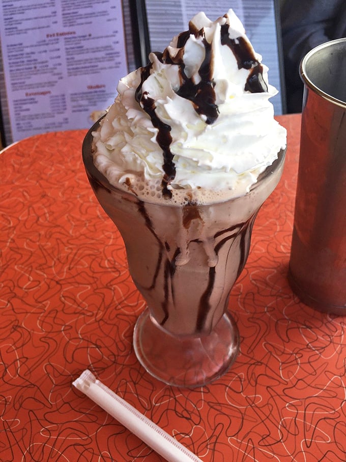 This isn't just a milkshake—it's a tower of whipped cream architecture that requires both a spoon and a strategy. Chocolate drizzle as art form.